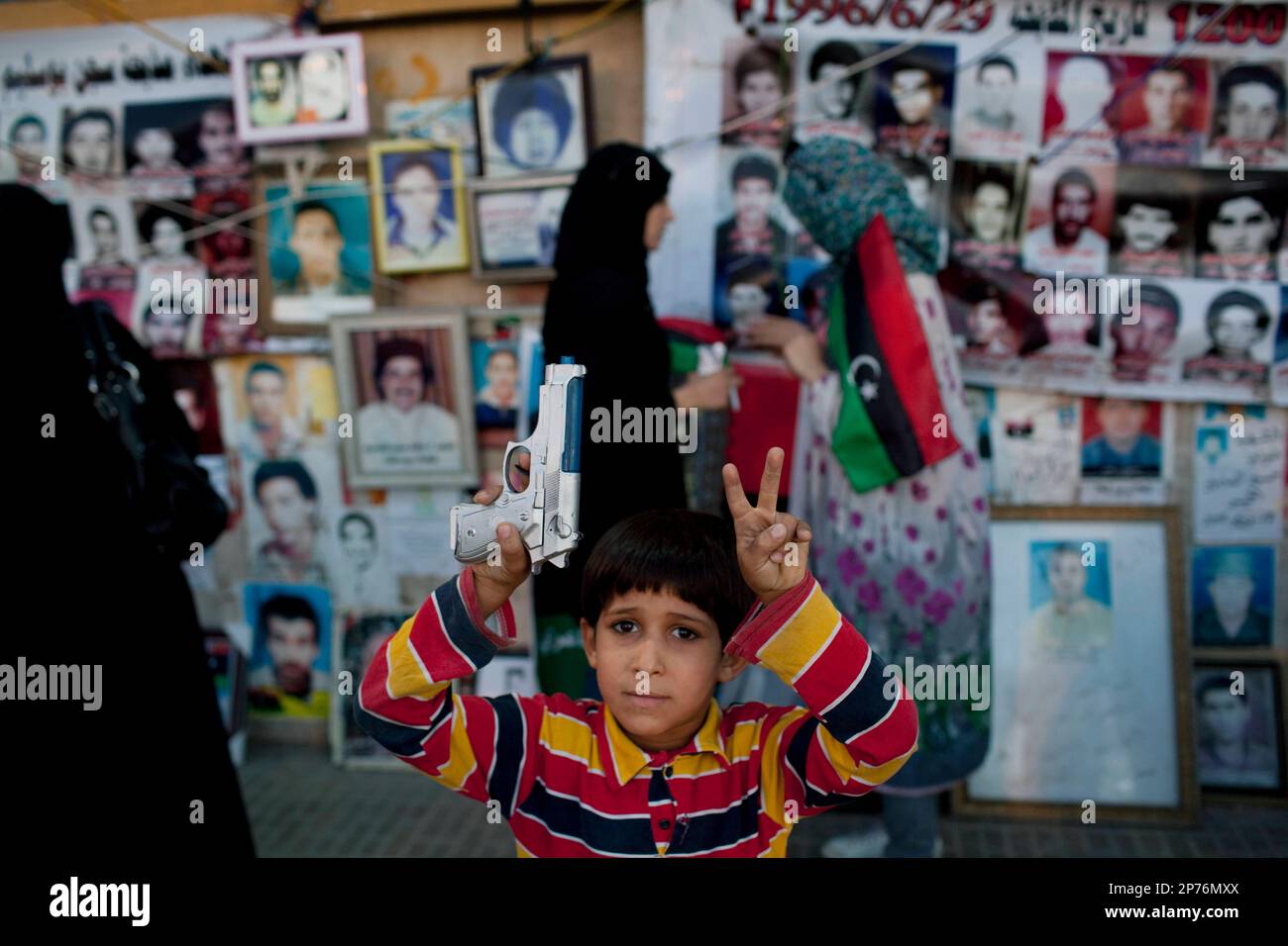 A boy holding a plastic weapon poses for a picture in front of portraits of people who were ...