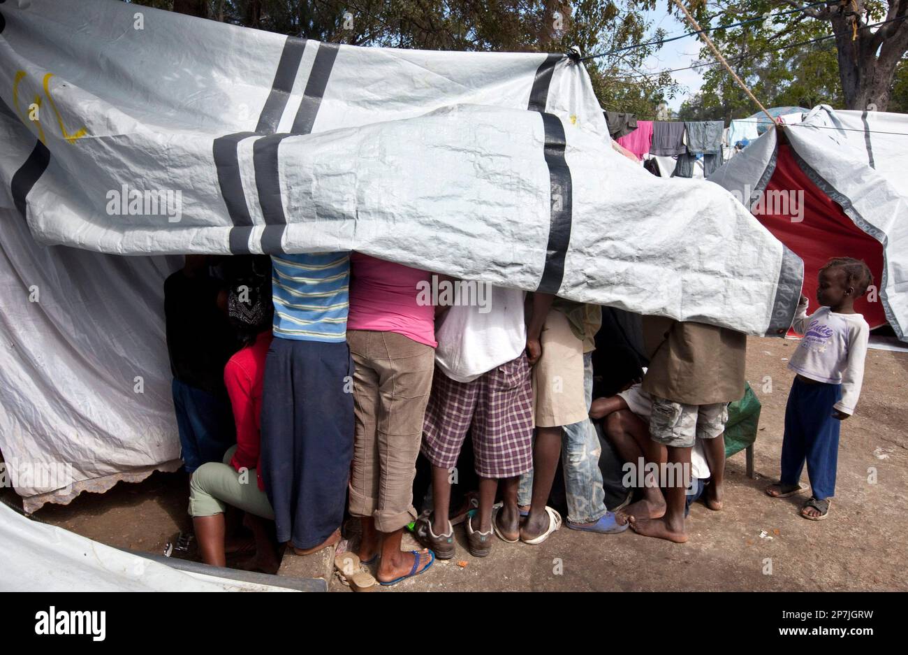 A group gathers under a tent to watch television in a displaced person ...