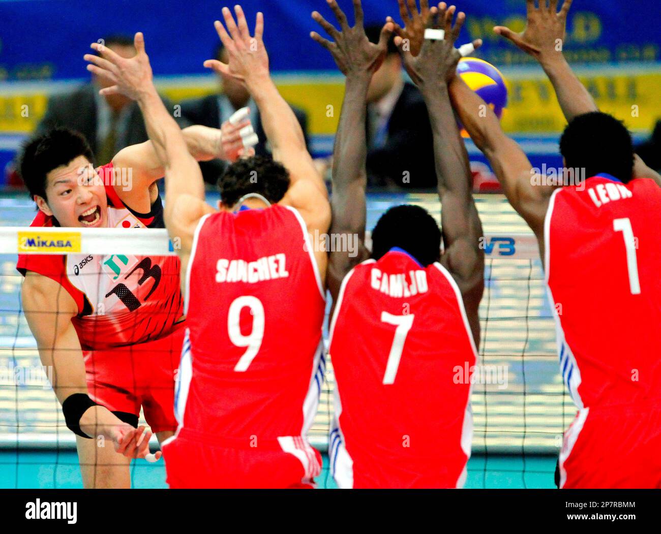 Kunihiro Shimizu, left, of Japan spikes the ball against Cuba's players Michael Sanchez Bozlueva ...