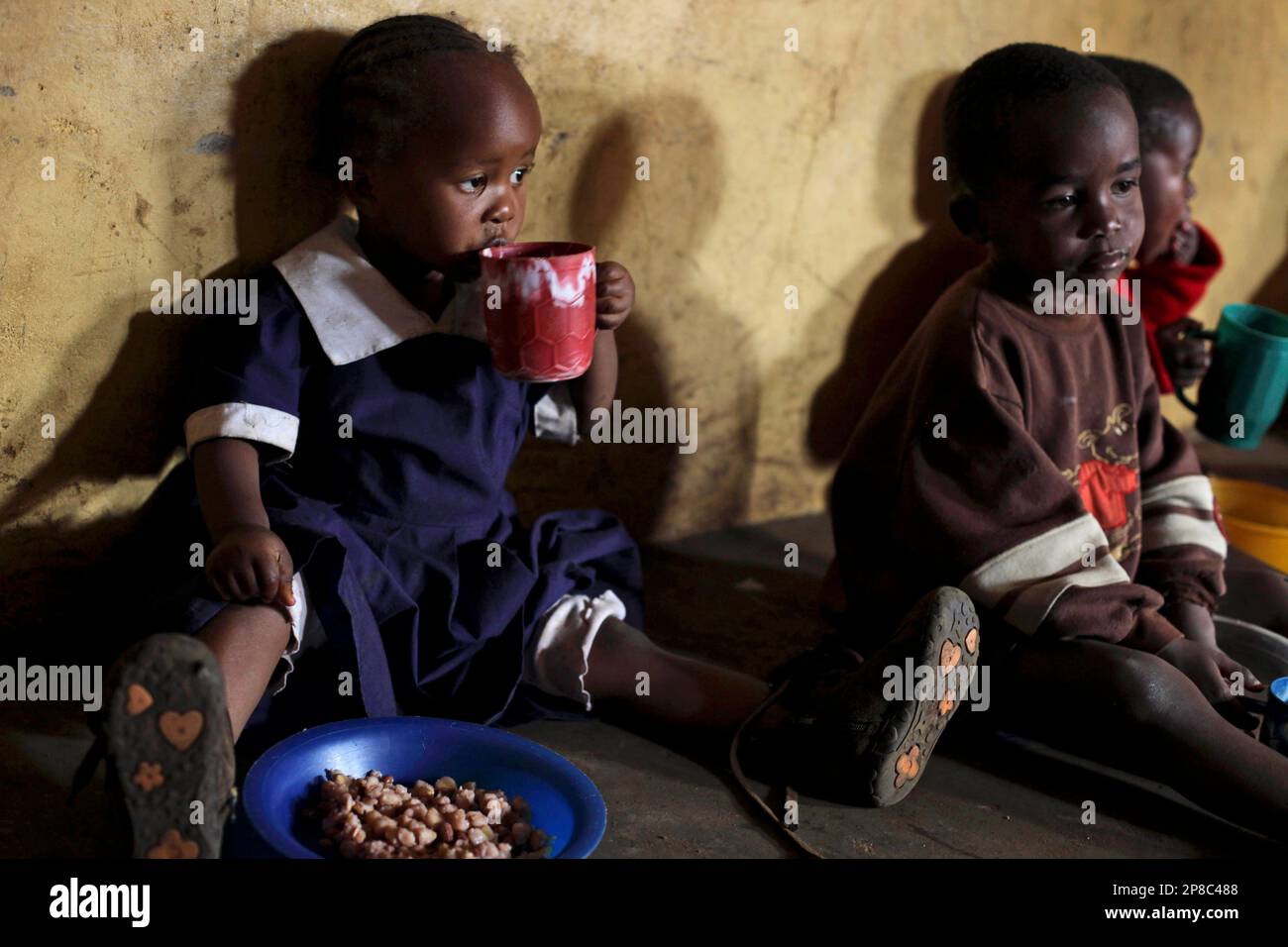A young child sips from a cup during lunch break in a makeshift school ...
