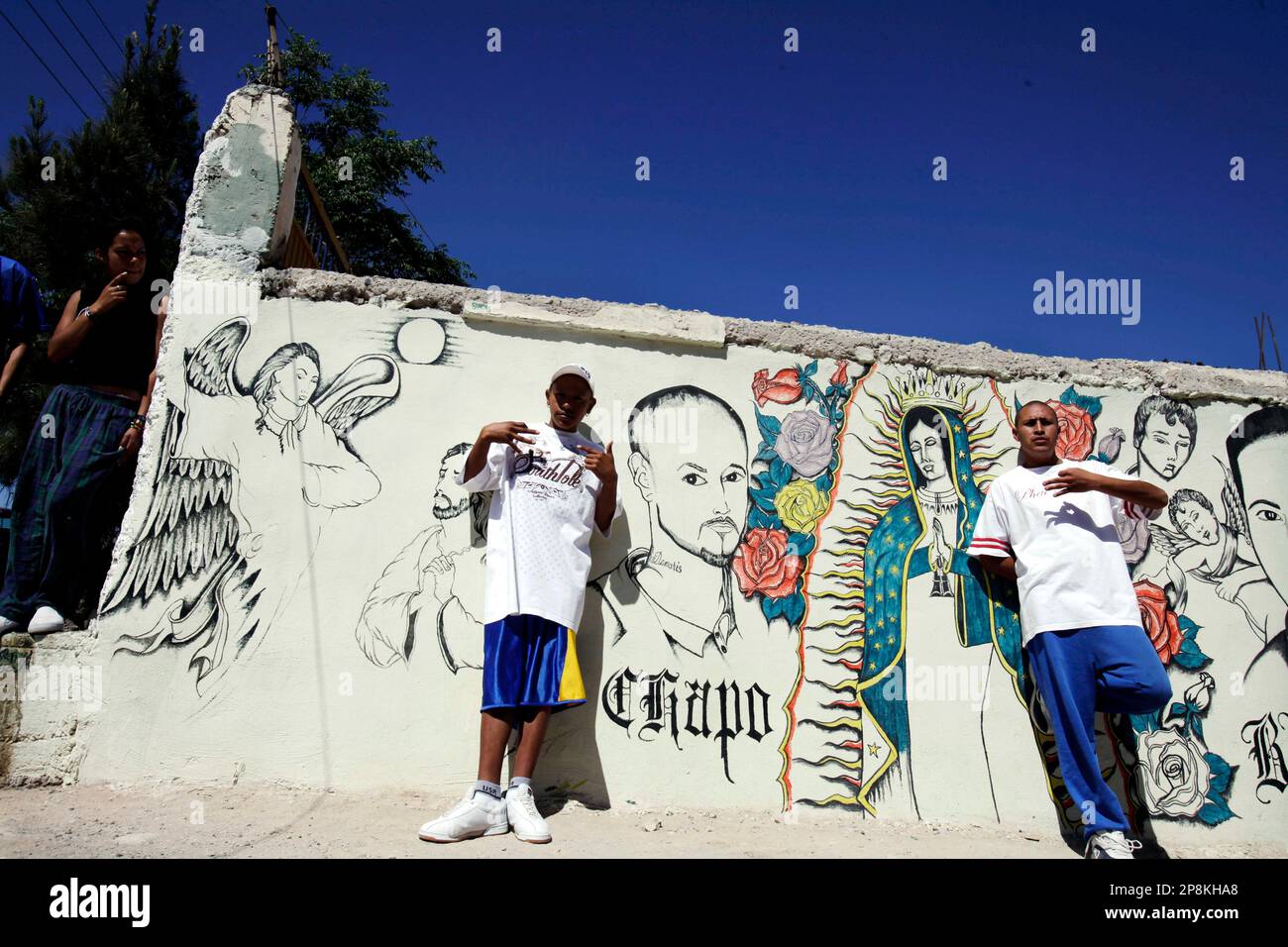 Gang members pose for pictures in front of graffiti depicting dead ...