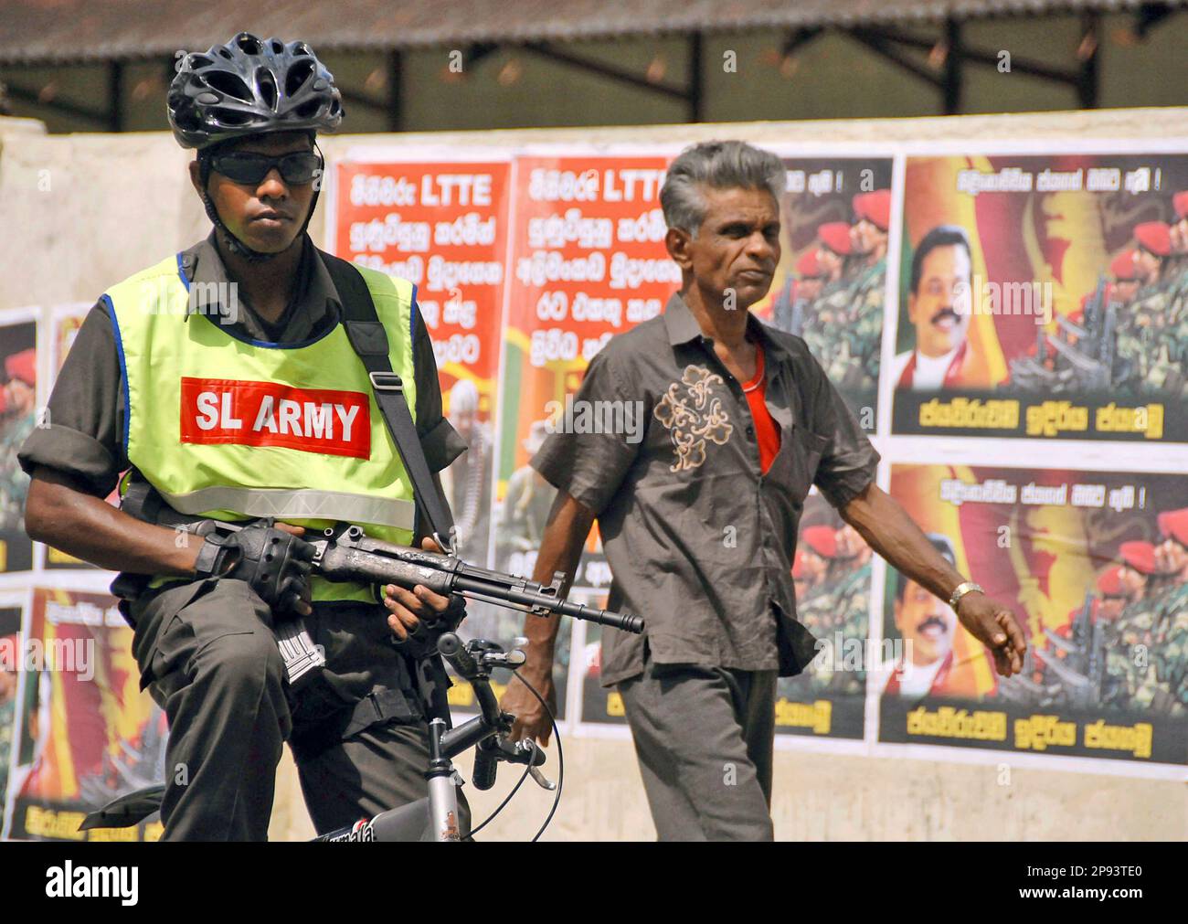 An armed Sri Lankan soldier on a bicycle stands guard as a civilian ...