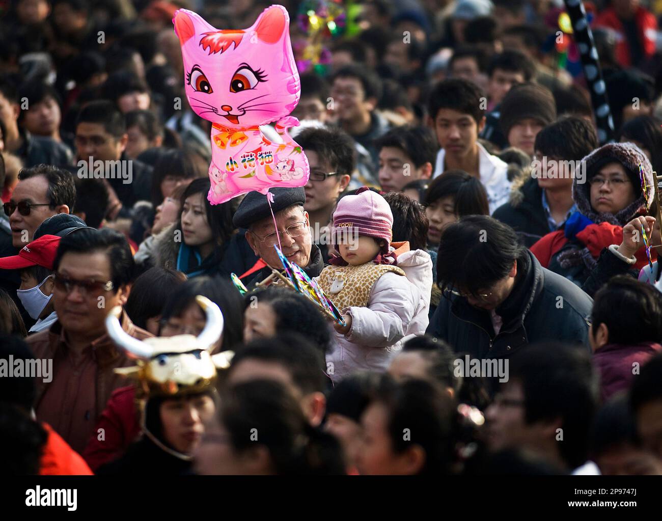 An elderly man, center, carries his grandchild as they walk among the ...