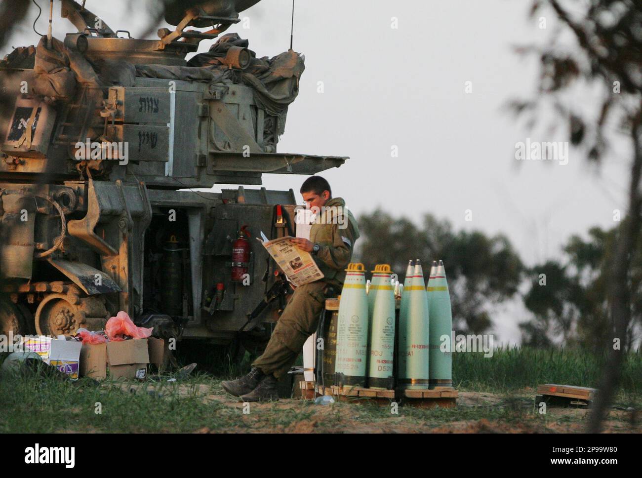 An Israeli soldier leans against artillery shells while reading the ...