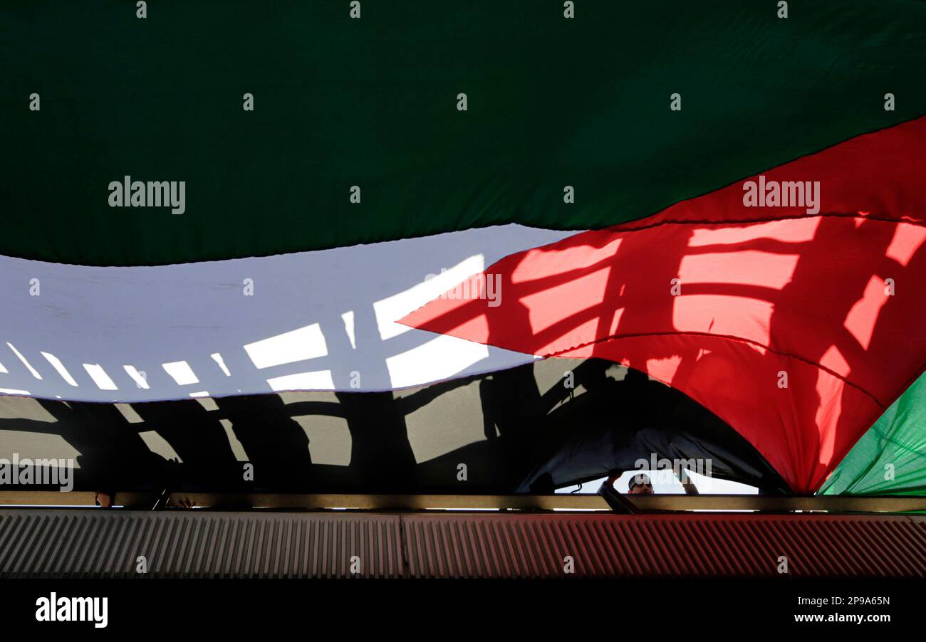 Palestinian protesters standing on a bridge wave a huge Palestinian ...