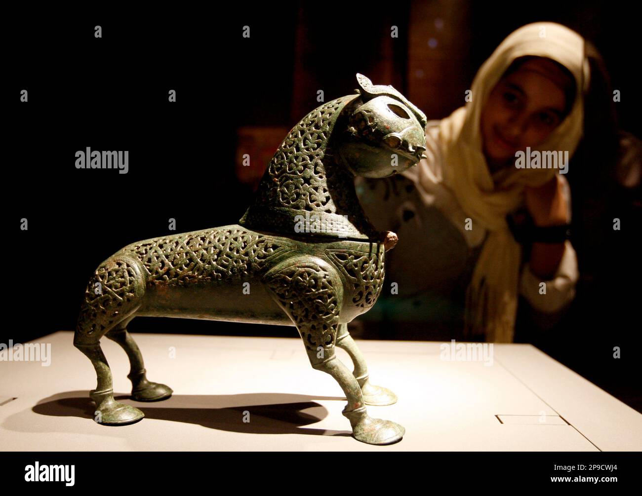 A Qatari girl looks to an Iranian Incense burner in the form of a lion ...