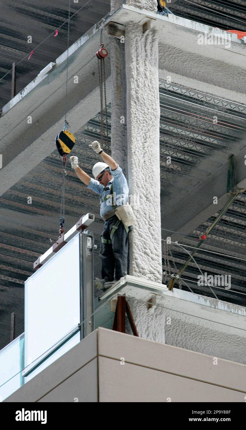 A construction worker directs a crane operator to position a window at ...