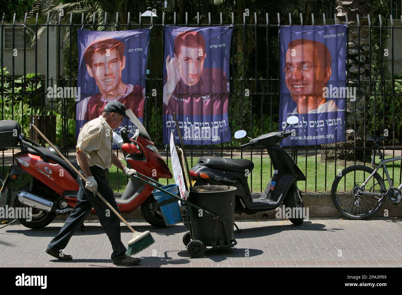 A street cleaner walks next to posters showing the portraits of Ehud ...