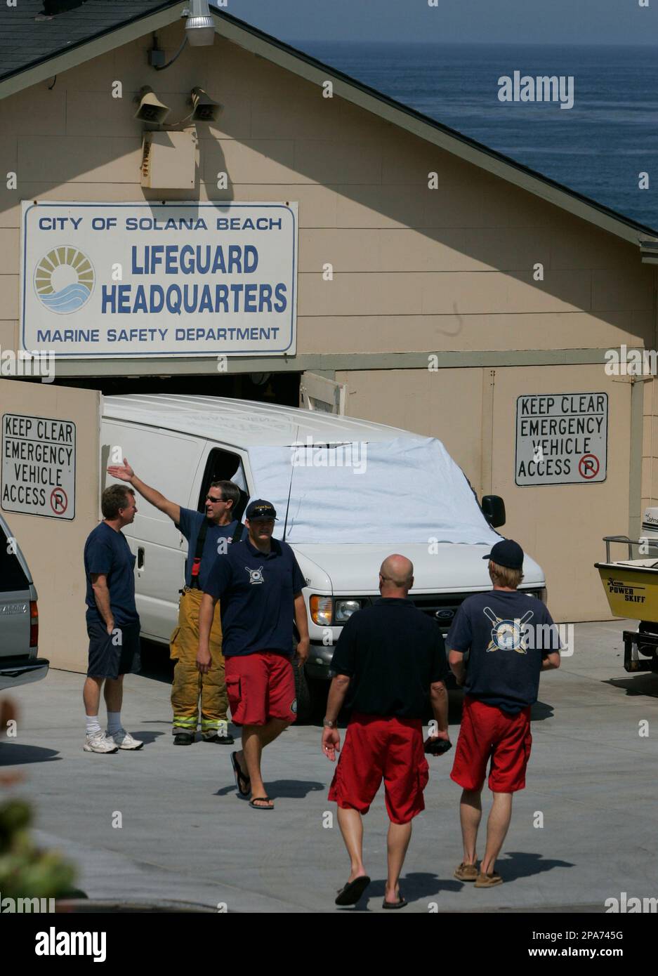 A lifeguard and fire department members stand next to a coroners van ...