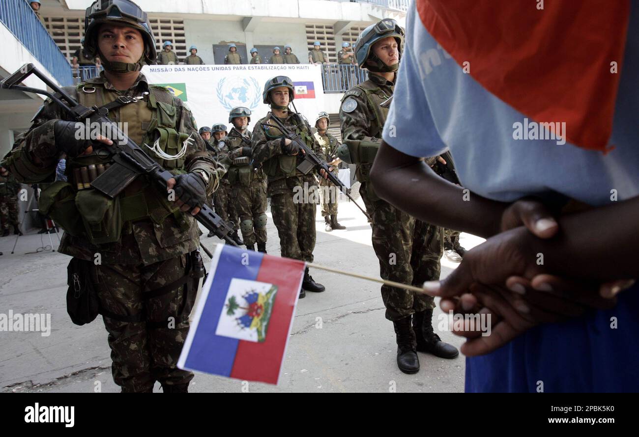 A child holds a Haitian flag as U.N. peacekeepers stand by during a ...