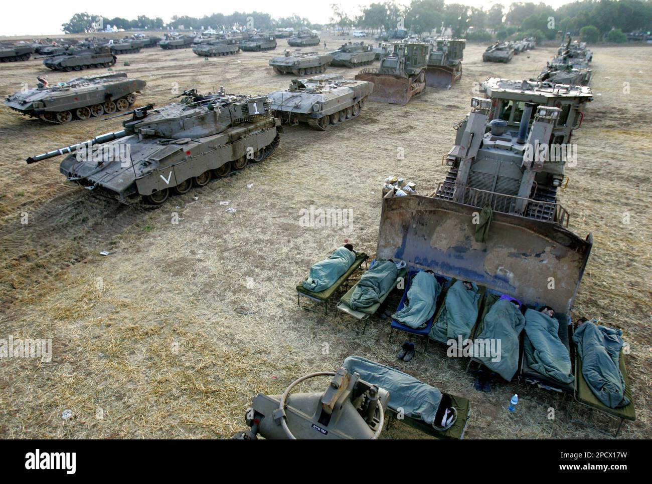 Israeli soldiers sleep next to armored vehicles at a gathering point ...