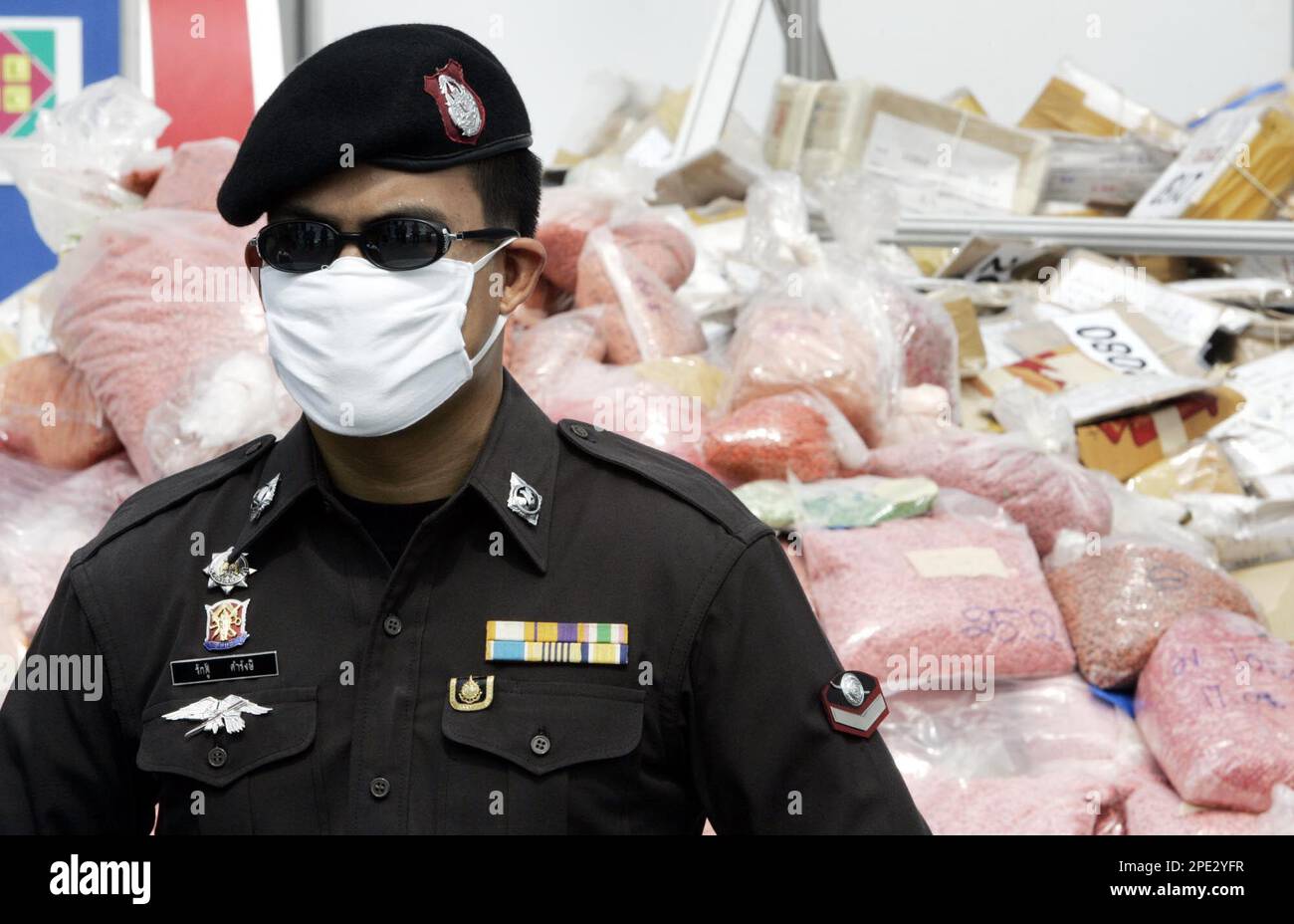 A Thai police officer stands guarding a pile of packs of ...