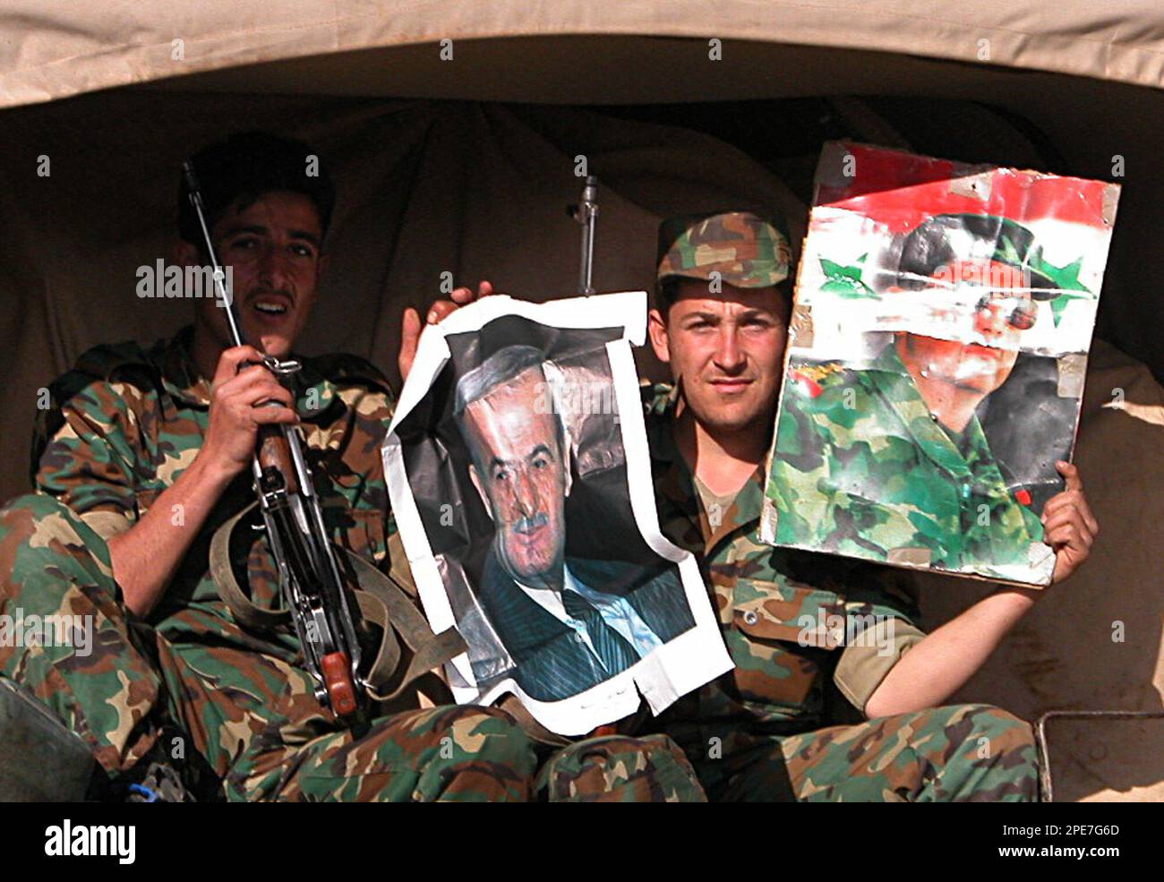 Two Syrian soldiers sit on a military truck holding portraits of late ...