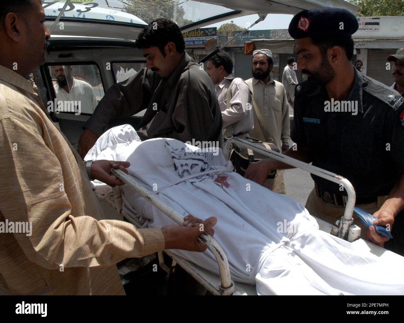 A Pakistani police officer and hospital staff load the dead body of a ...