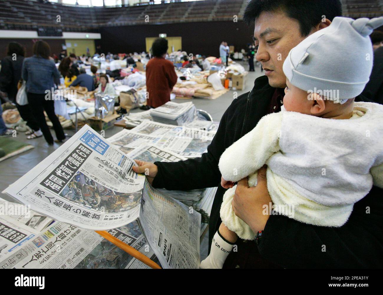Evacuee Akio Sumihiro, holding his son Asahi, reads a front page story on the earthquake in a ...