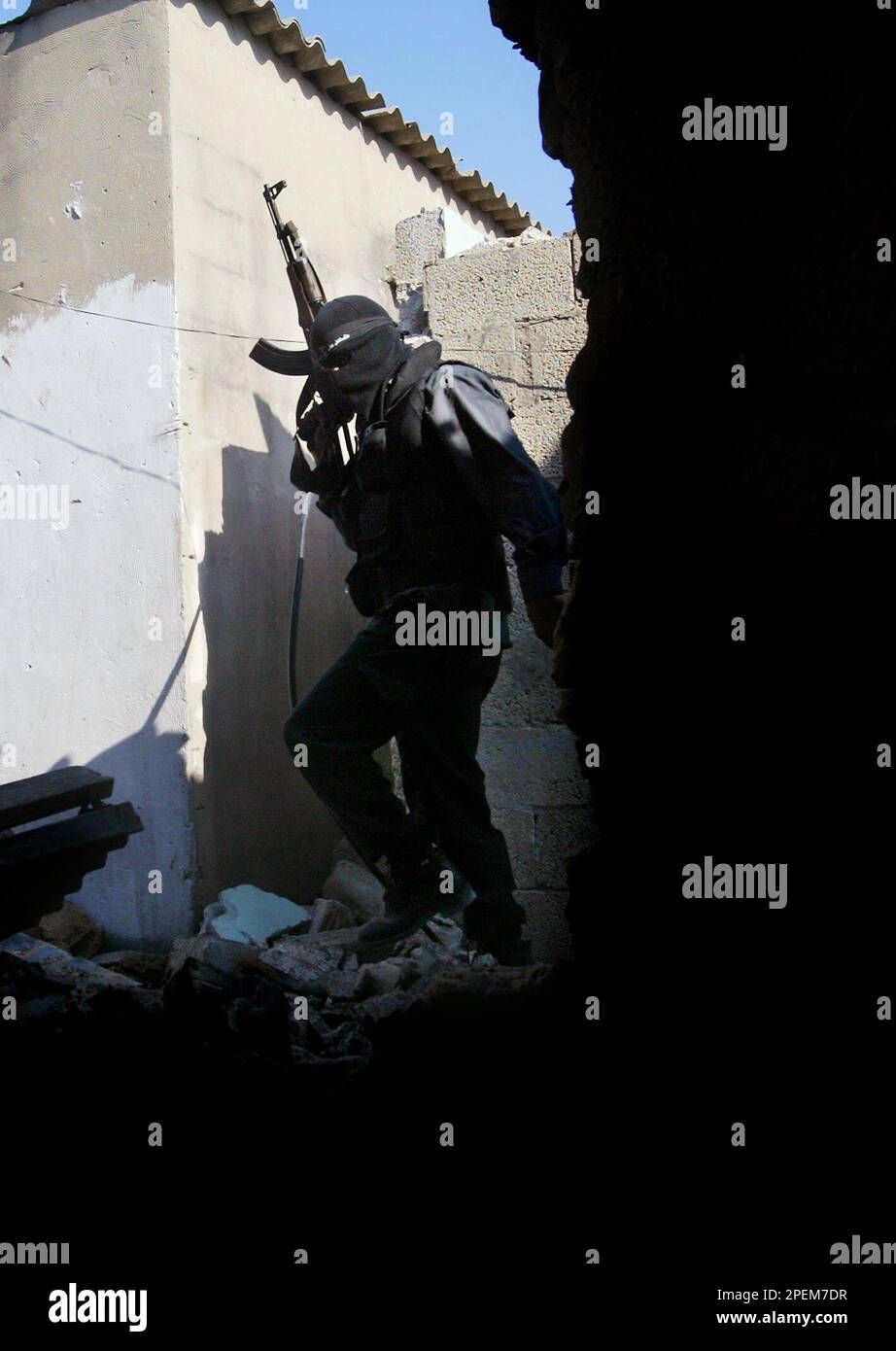 A Palestinian masked militant walks through the rubble of a house ...