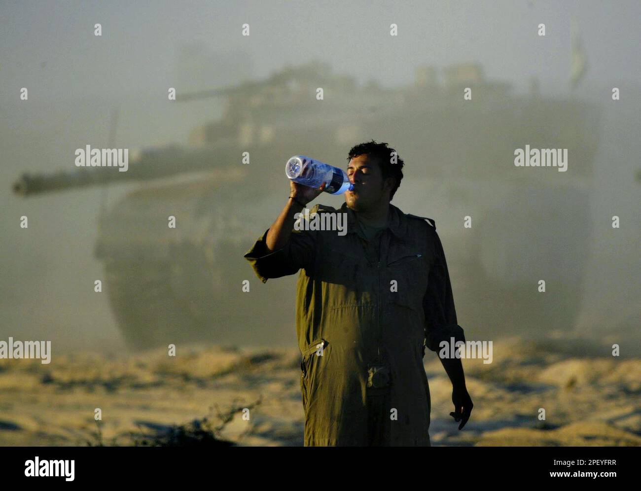 An Israeli soldier drinks water as a tank manoeuvres in the background ...