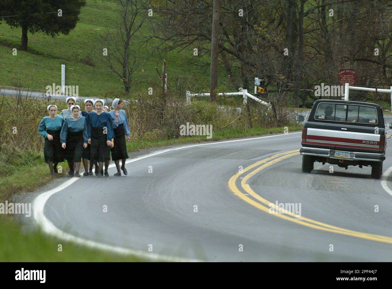 Amish teenage girls walk on the shoulder of a road as a pickup truck ...