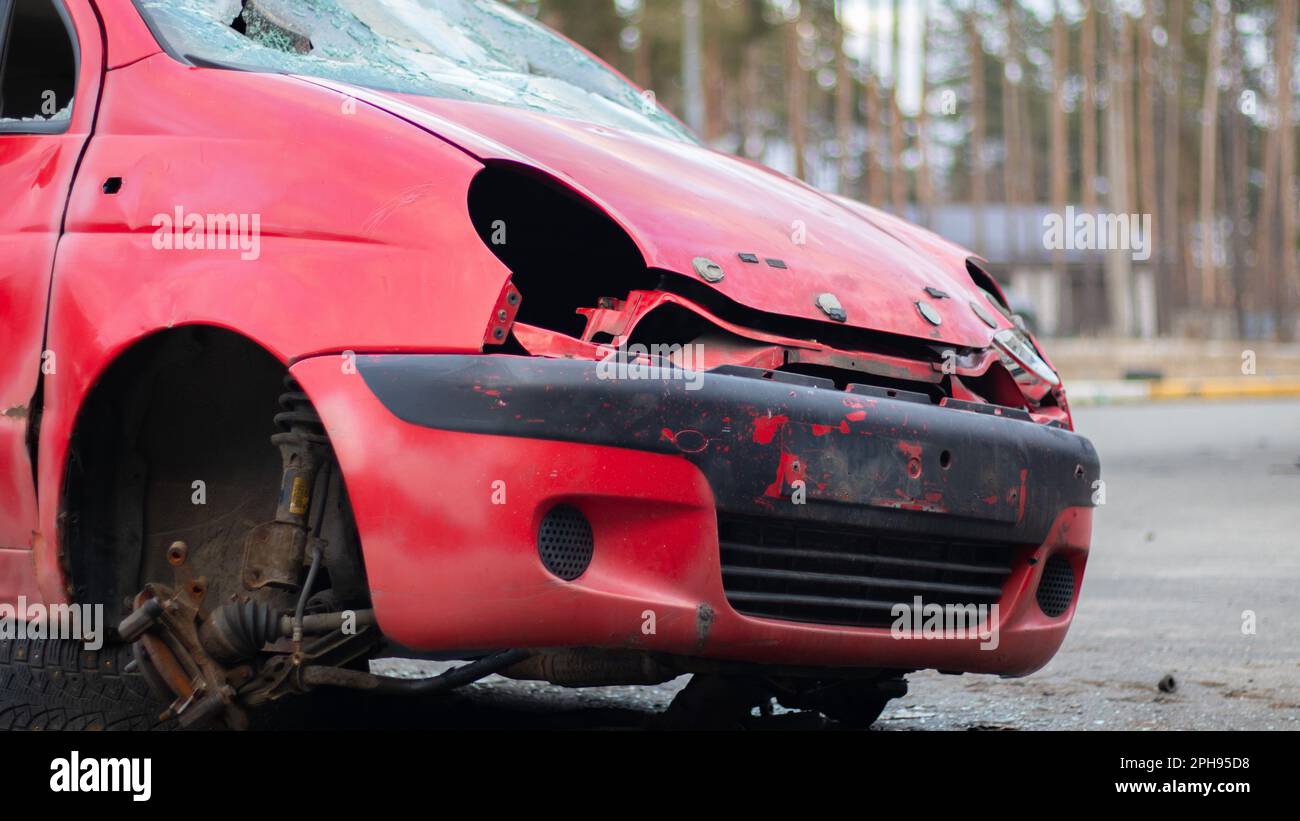 Ein zerbrochenes, rotes Auto steht am Straßenrand ohne Scheinwerfer und ...