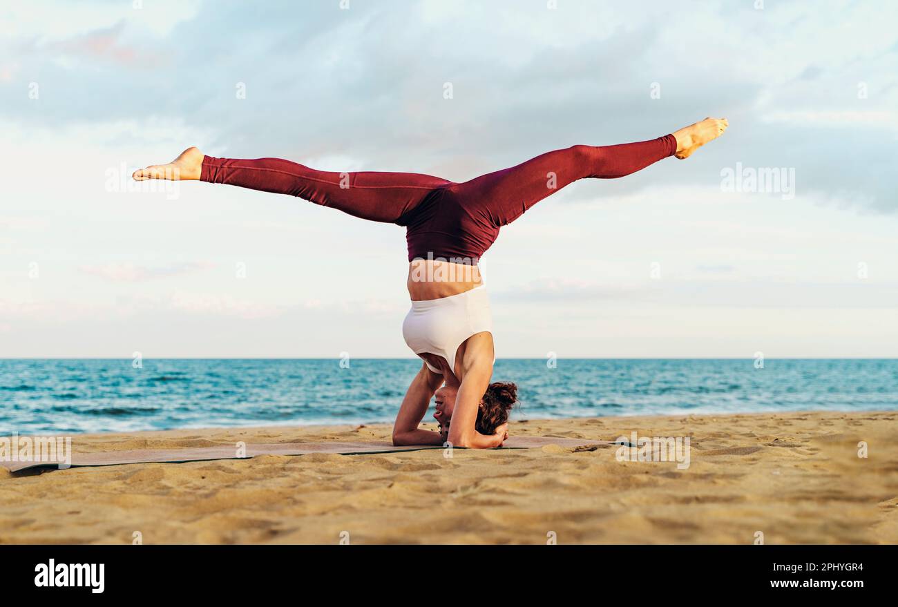 Eine junge weiße Frau in Sportbekleidung übt bei Sonnenuntergang Yoga ...