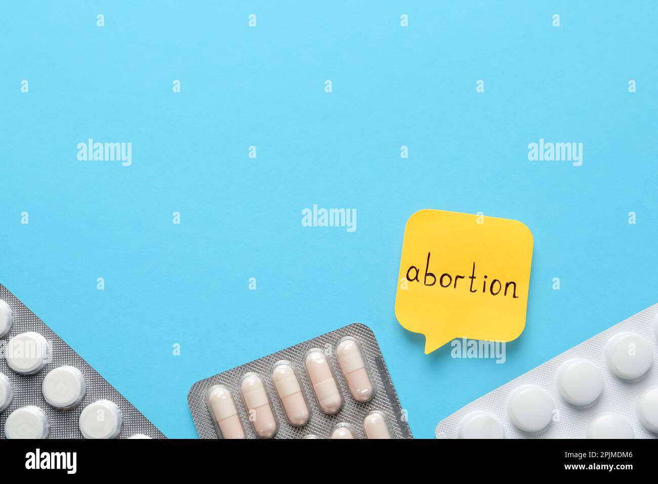 Papierbrief mit Wort Abtreibung und Pillen auf hellblauem Hintergrund, flach liegend. Platz für ...