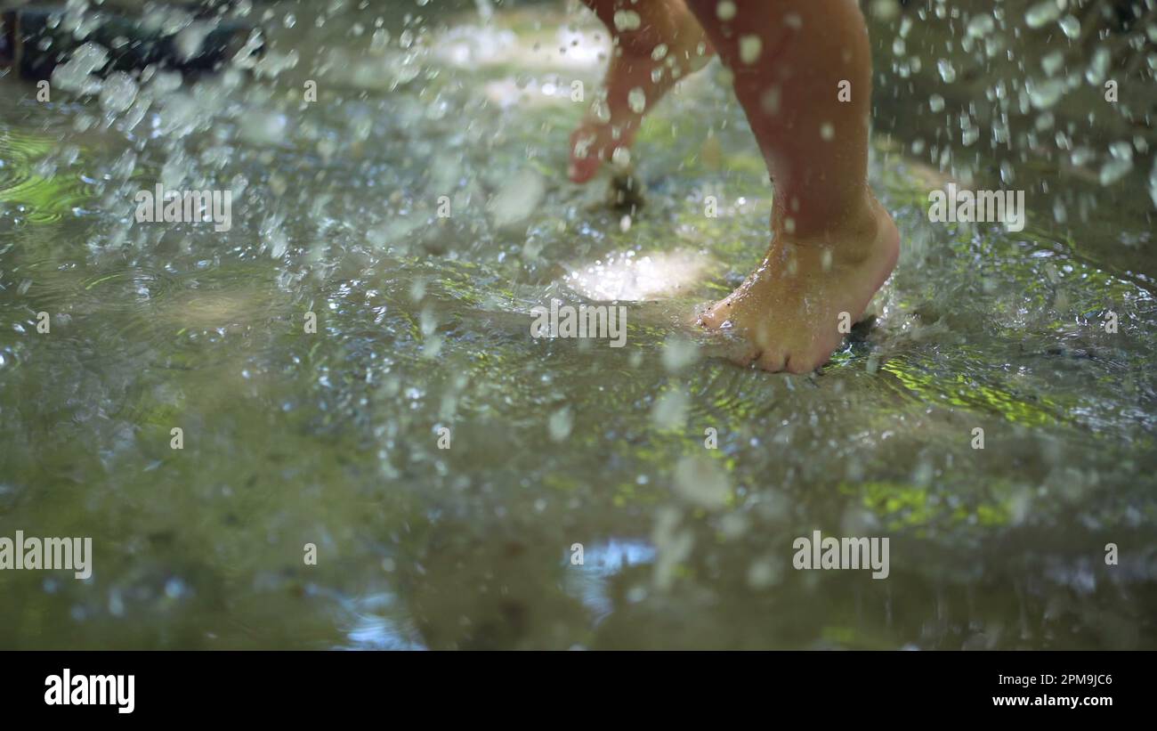 Ein kleiner Junge, der im Park ins Wasser springt. Kind spritzt Wasser ...