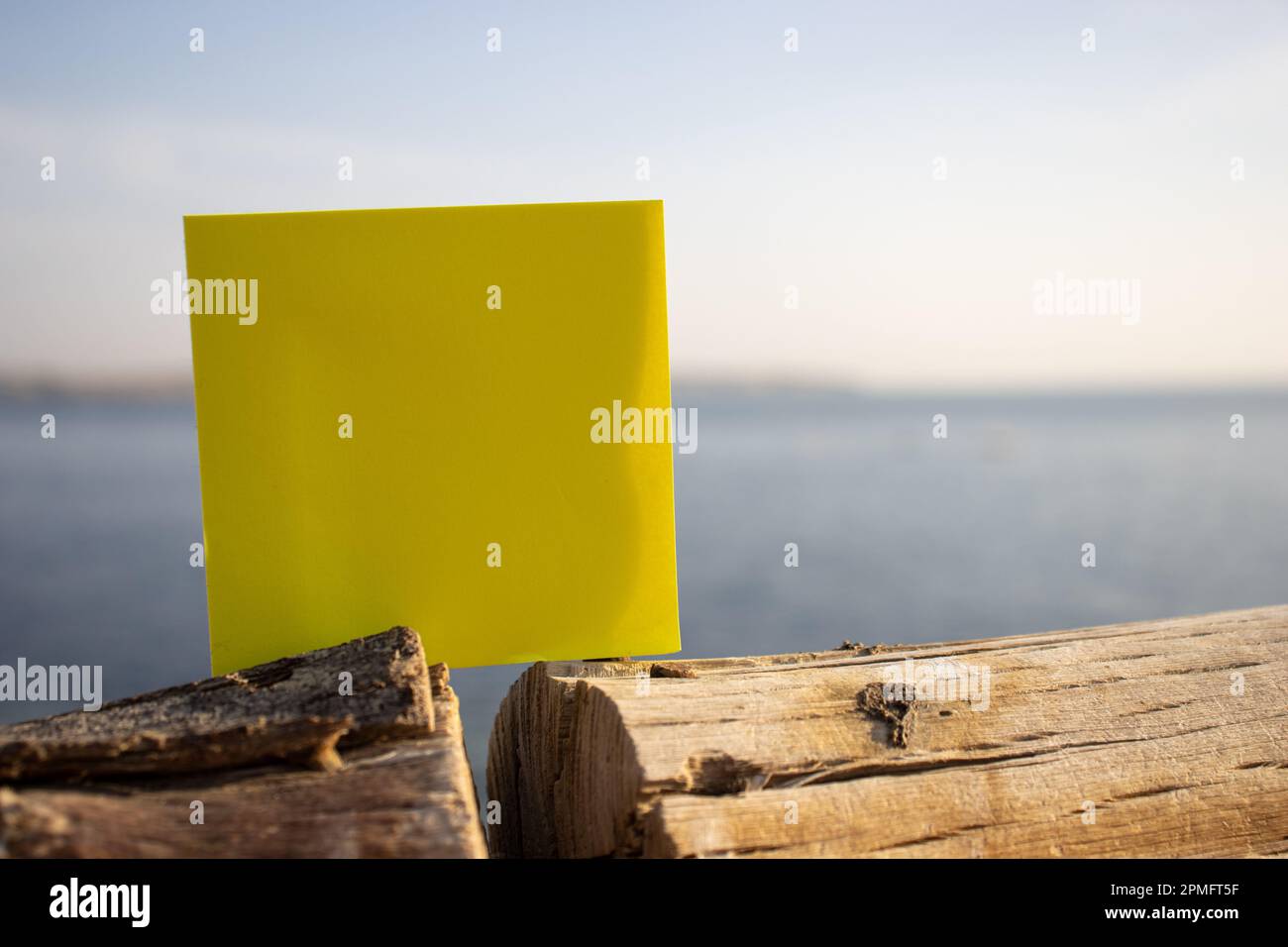 Gelber quadratischer Zettel, der im Riss eines runden Holzzauns ruht ...