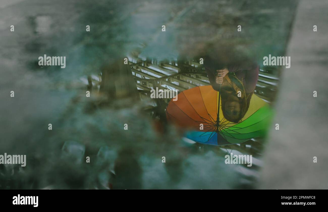 Regenbogen-Regenschirm-Reflexion in der Pfütze auf der Straße der Stadt ...