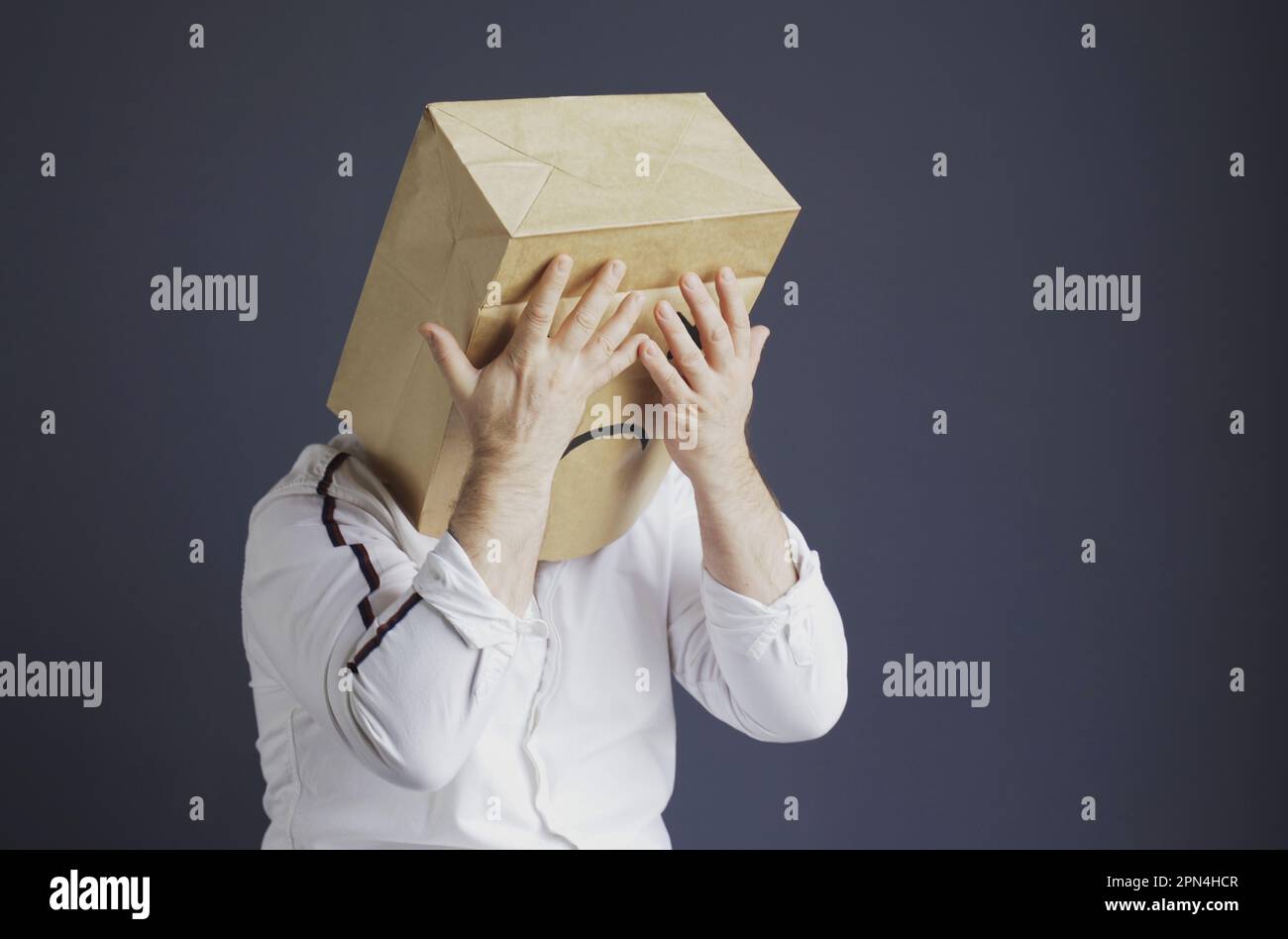 Ein trauriger Mann in einem weißen Hemd mit einer Tasche auf dem Kopf, mit einem gezeichneten ...