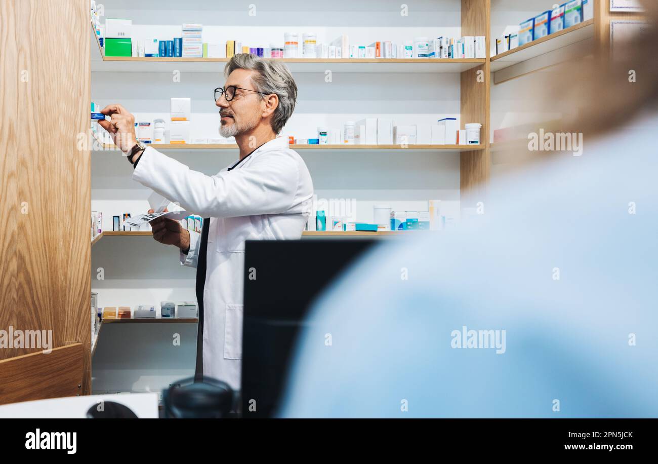Männlicher Apotheker, der einem Patienten mit einem Rezept in einer Apotheke hilft. Senior ...