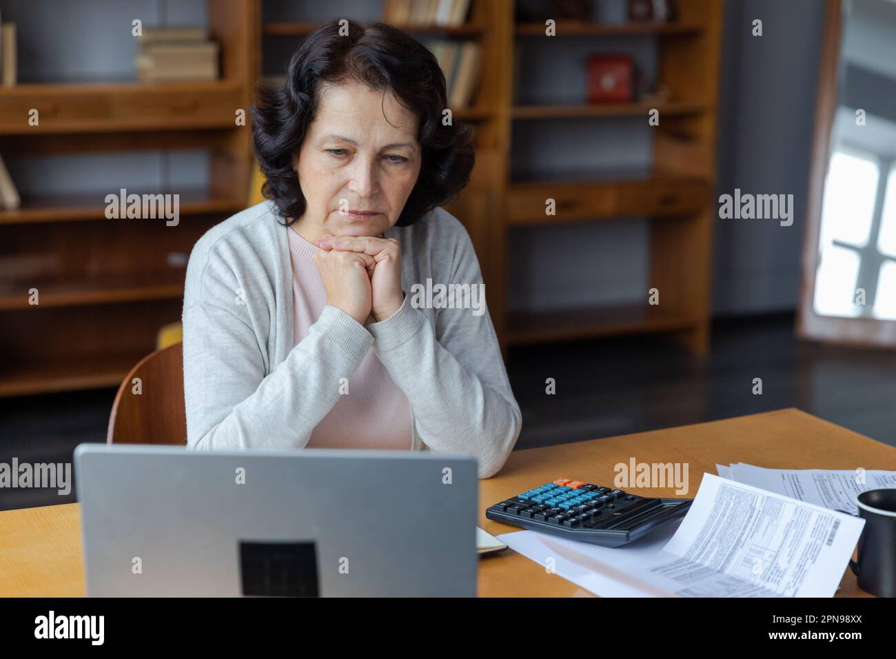 Eine ältere Frau im mittleren Alter sitzt mit einem Laptop und einem ...