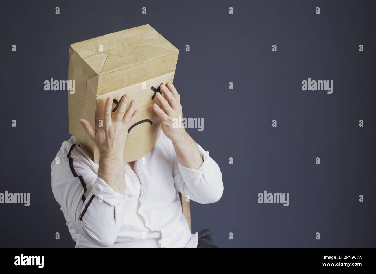 Ein trauriger Mann in einem weißen Hemd mit einer Tasche auf dem Kopf, mit einem gezeichneten ...