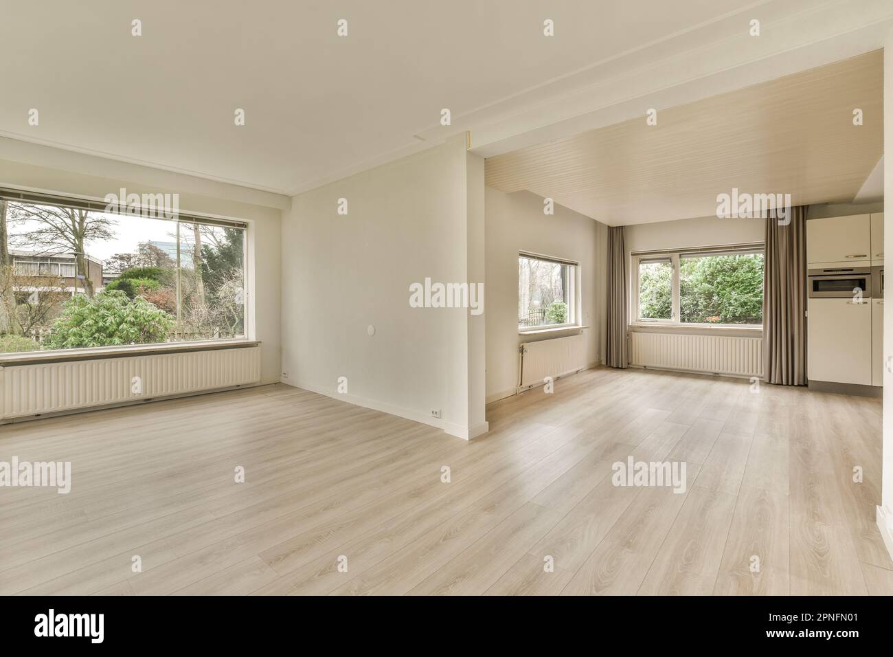 Ein leeres Wohnzimmer mit Holzfußboden und großen Fenstern mit Blick auf den Garten draußen auf ...