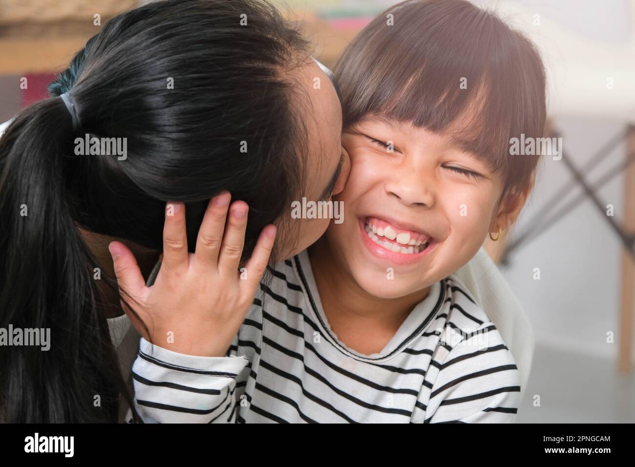 Mutter und ihre Tochter spielen und umarmen. Lächelnde Mutter und lustige kleine Tochter, die zu ...