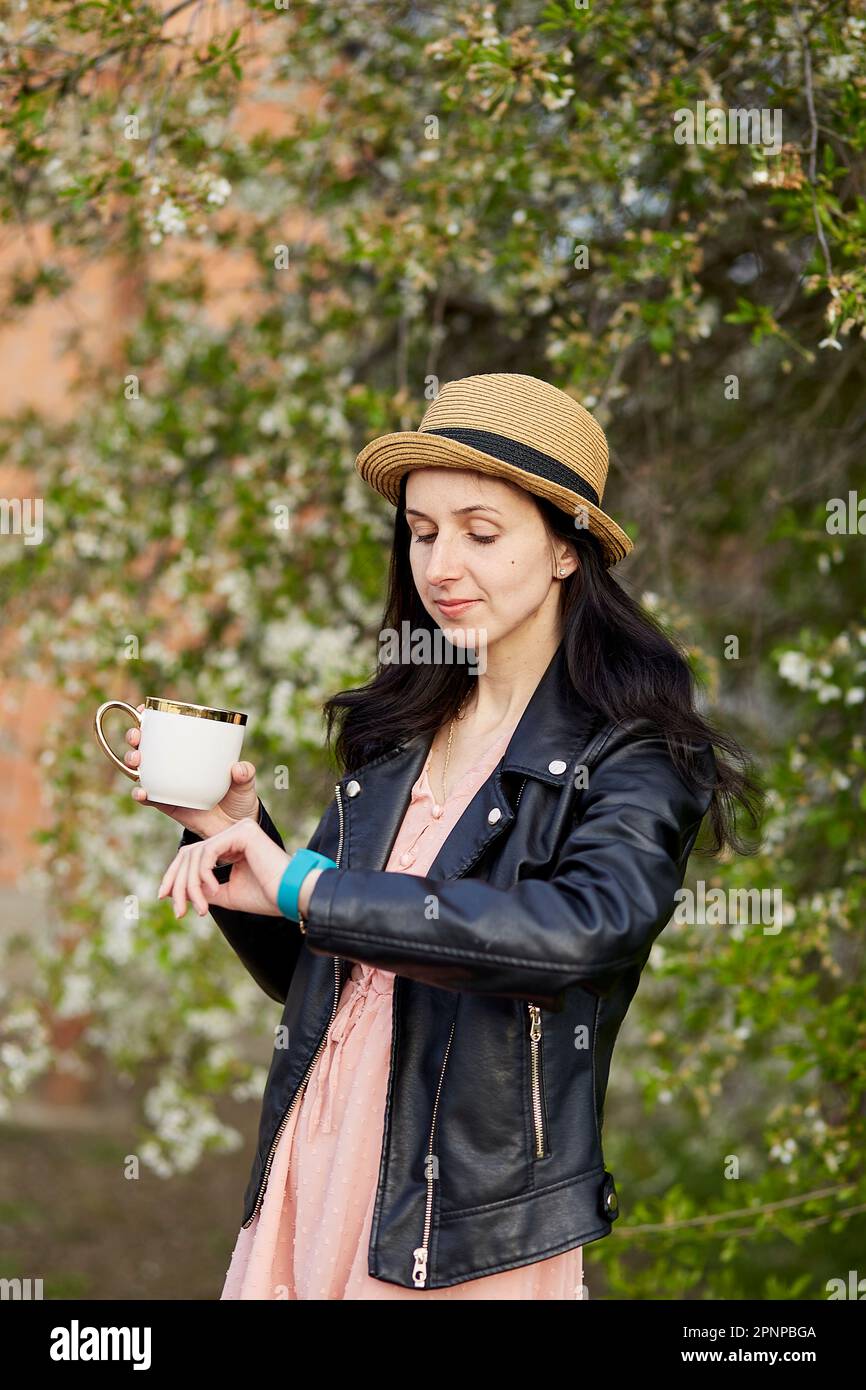 Eine Frau mit einer Tasse Kaffee neben einem blühenden Baum, schauen ...