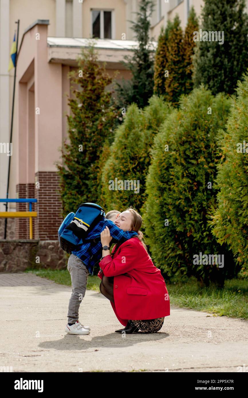 Junge Mutter sieht das Kind zur Schule und umarmt sich zum Abschied ...