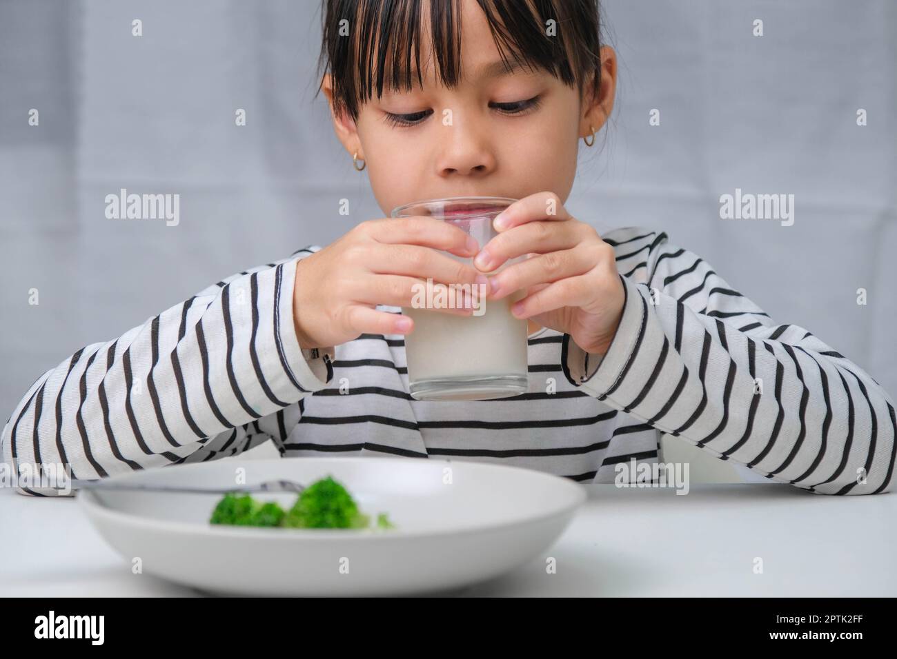 Süßes asiatisches Mädchen, das morgens ein Glas Milch trinkt, bevor es ...