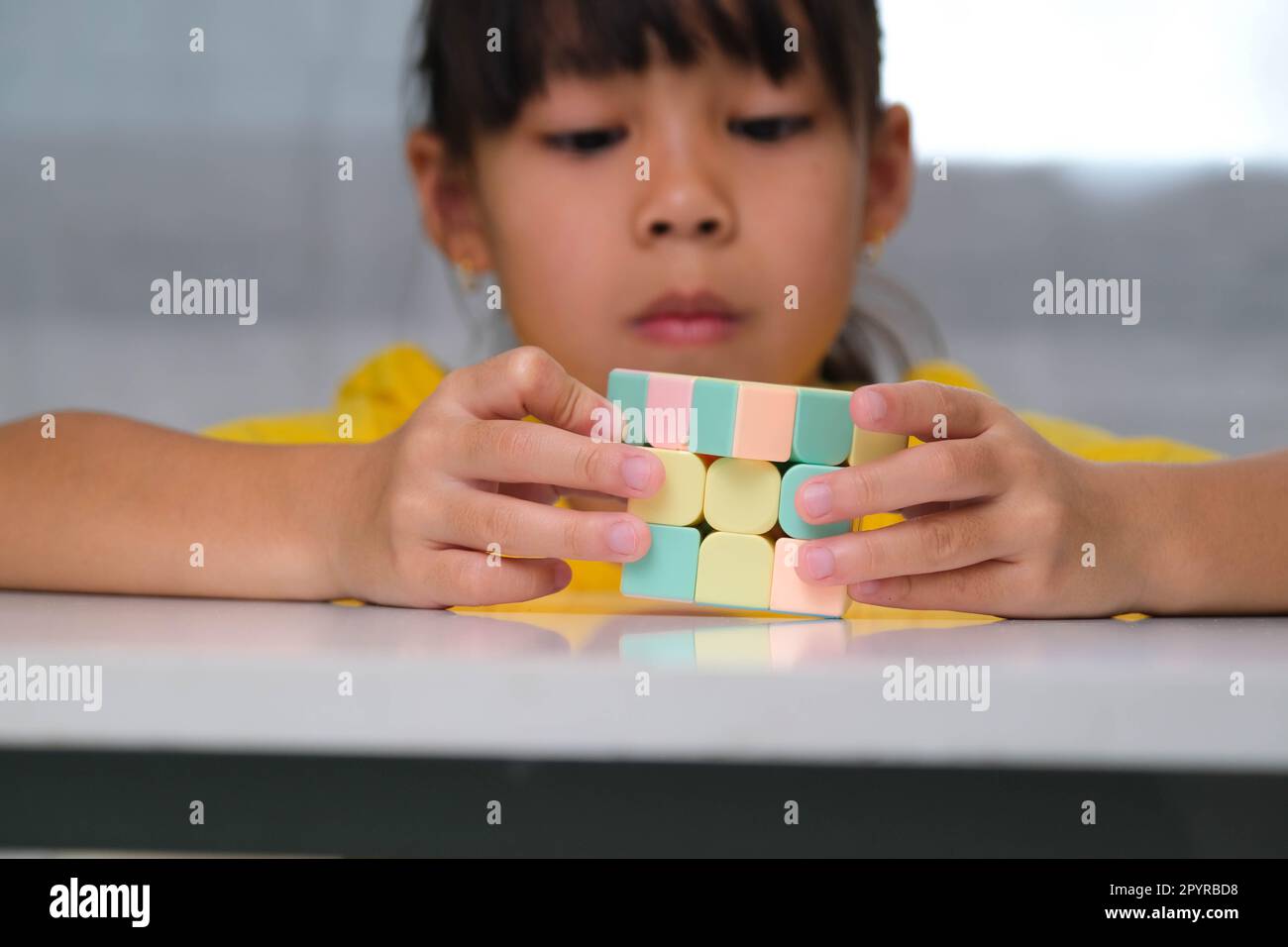 Asiatisches, süßes Mädchen, das Rubiks Würfel in der Hand hält und damit spielt. Rubiks Würfel ...