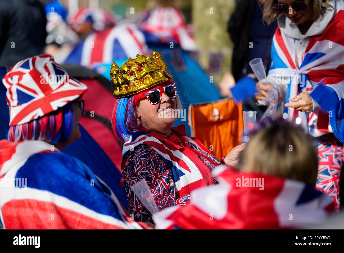 Members of the public wearing Union Jack colours sit in the sunshine on ...