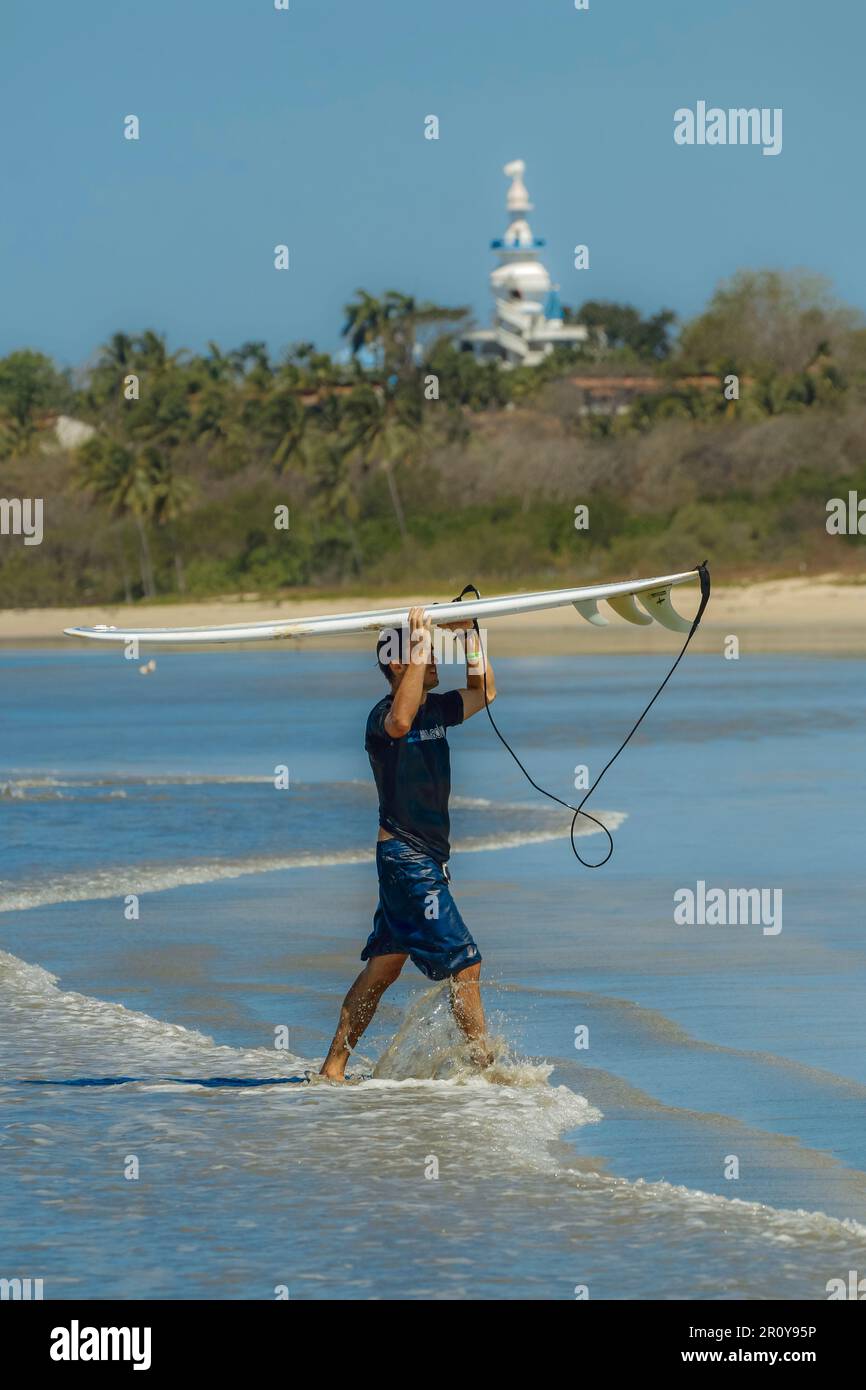 Surfer mit Brett auf dem Kopf und das Nosara Beach Hotel dahinter an ...