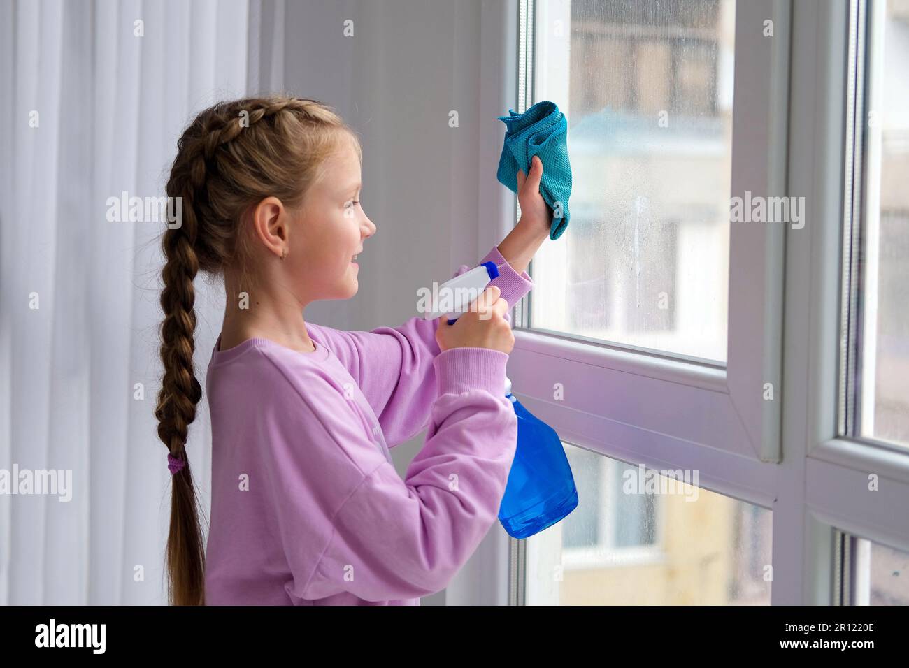 Ein kleines Mädchen in einem violetten Pullover streut Wasser aus einer ...