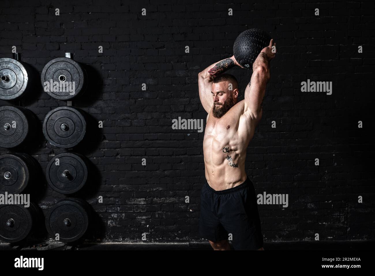 Junger aktiver, starker, schweißtreibender, fokussierter Mann mit großen Muskeln hält schwere ...