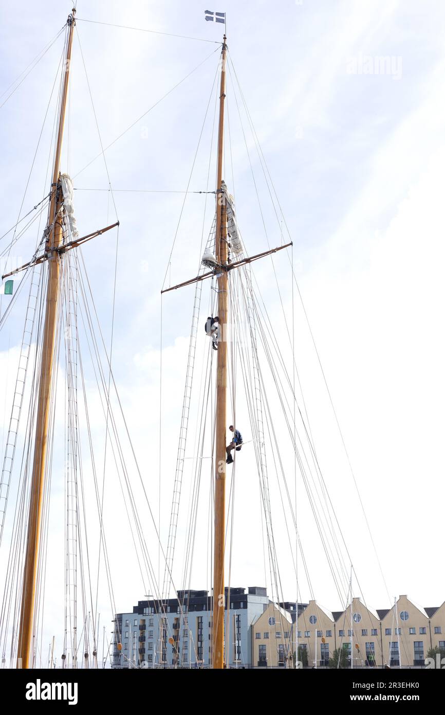 Zwei Männer baumeln sehr hoch, während sie auf einem hohen Mast eines ...