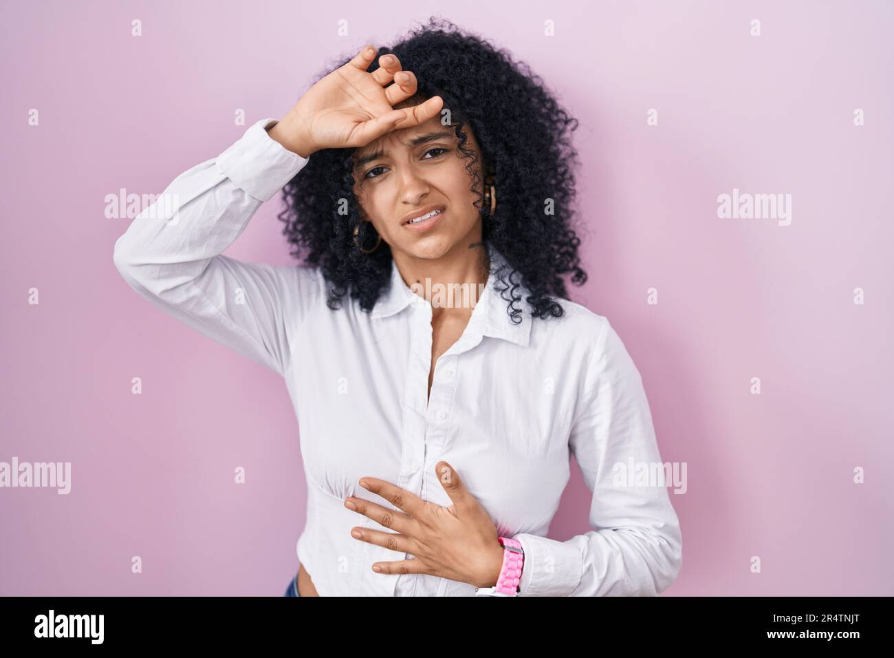 Hispanische Frau mit lockigem Haar steht über rosa Hintergrund und ... Hispanische Frau mit lockigem Haar steht über rosa Hintergrund und ...