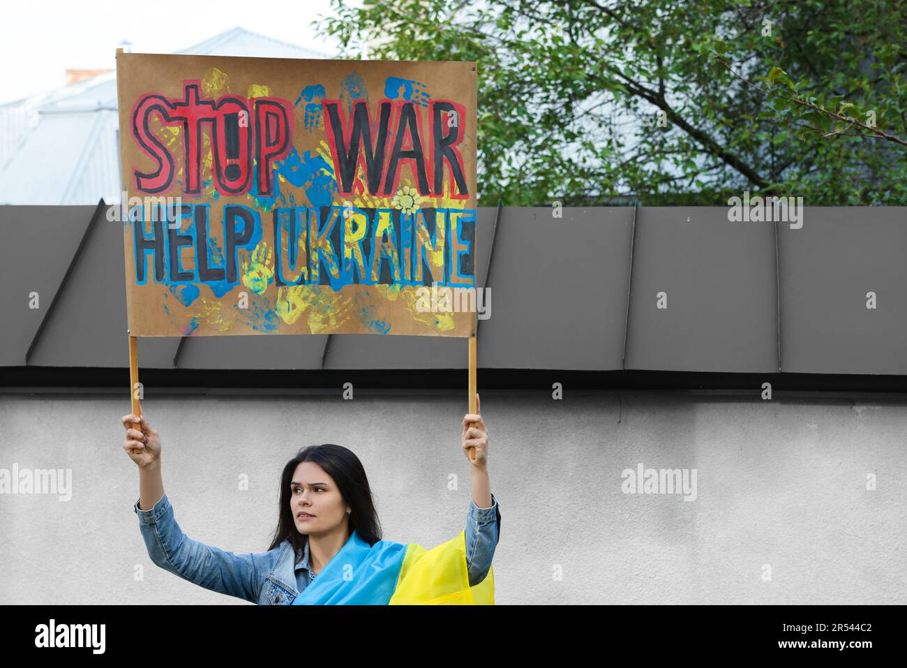 Traurige Frau, die in die ukrainische Flagge eingewickelt ist und ein Plakat mit Worten hält ...