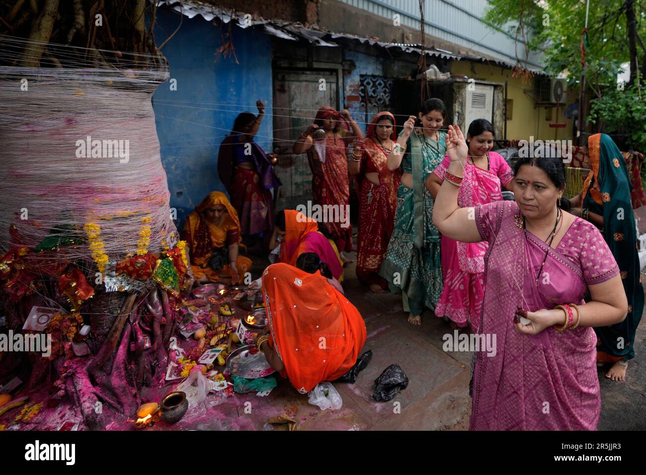 Married Hindu women tie a cotton thread around a Banyan tree as they ...