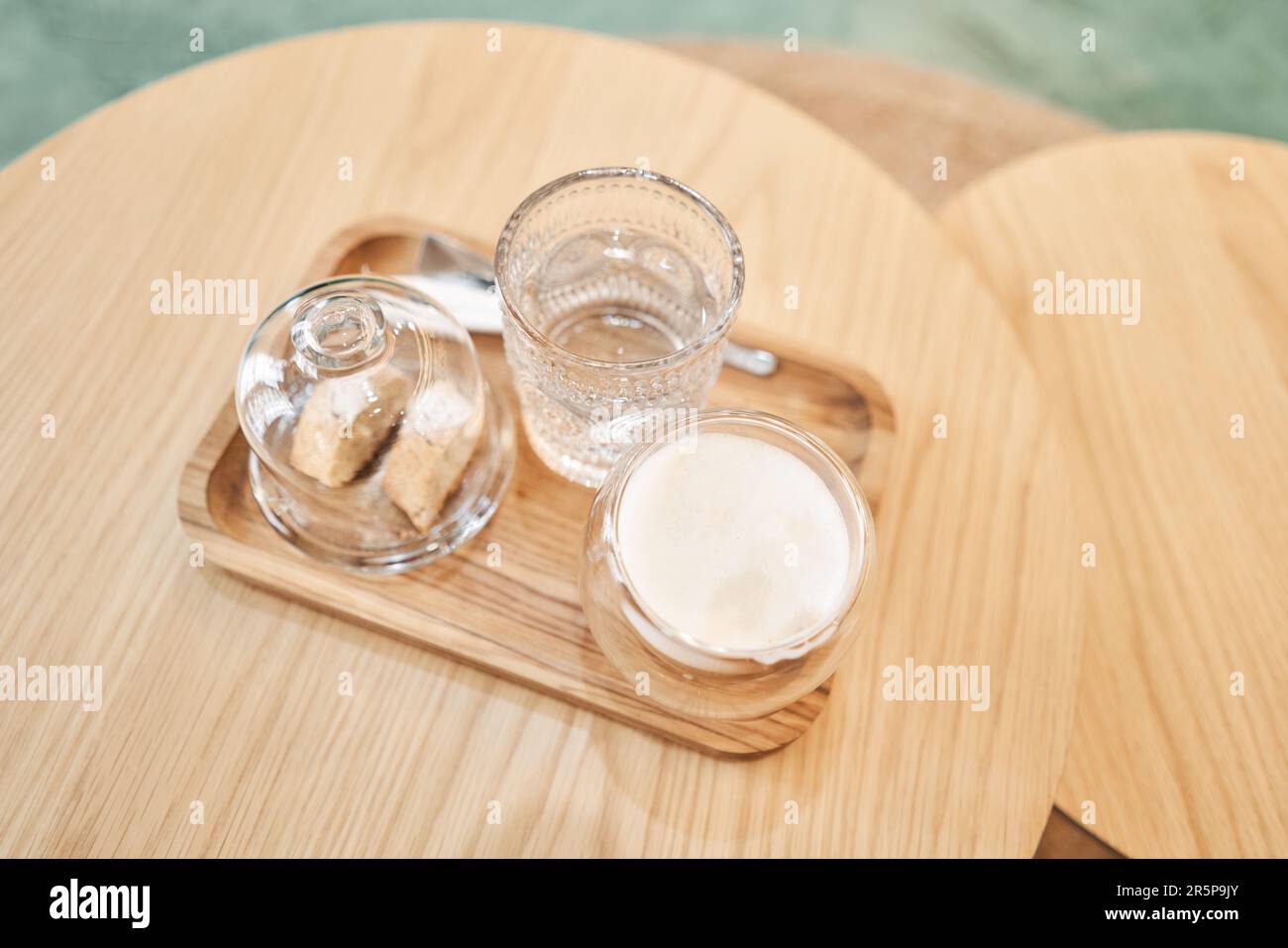 Kaffee mit Milch, ein Keks und ein Glas Wasser auf einem Holztisch ...