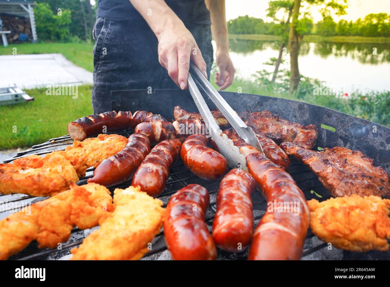 Ein Mann, der die Wurst auf den grill dreht, mit einer Küchenzange ...