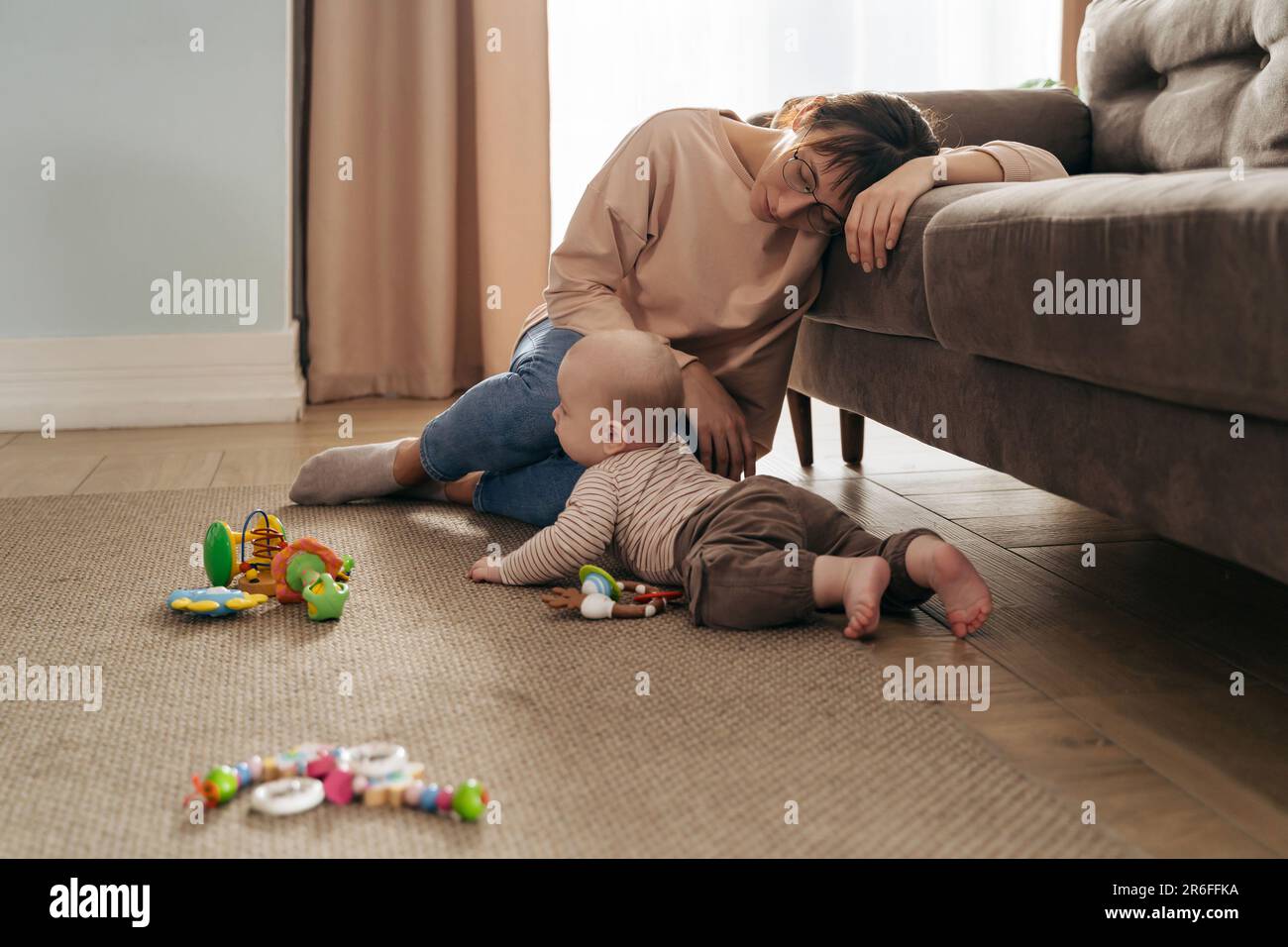 Junge erschöpfte Mutter ist sehr müde, schlief auf dem Sofa neben ihrem ...