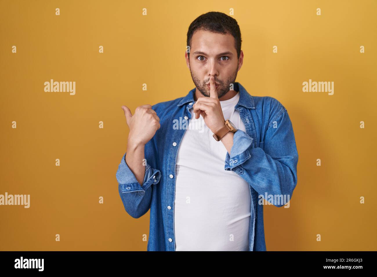 Lateinamerikanischer Mann, der auf gelbem Hintergrund steht und darum ...